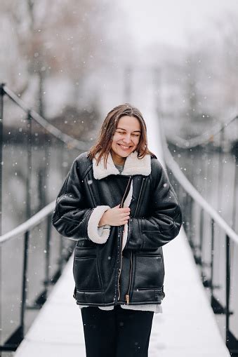 겨울날 한 여성이 현수교에서 강을 걷고 있습니다 따뜻한 옷을 입은 어린 소녀가 추운 눈 오는 날에 나무 인도교에 서 있다 25
