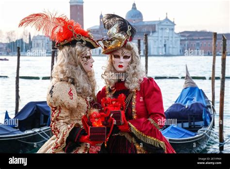 Two Women Dressed In Traditional Decorated Costumes And Painted Masks During The Venice Carnival