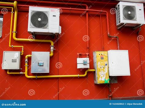Yellow Gas Pipes And Boxes On Vibrant Red Wall On A Residential House