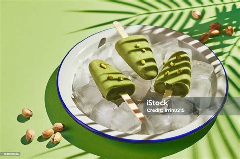 얼어붙은 홈메이드 피스타치오 아이스캔디가 녹색 배경에 얼음 그릇에 담긴 얼음 그릇에 담긴 야자수 잎 그림자를 거친 빛에 감습니다 상쾌한 아이스캔디 냉동 그린 주스를 스틱에