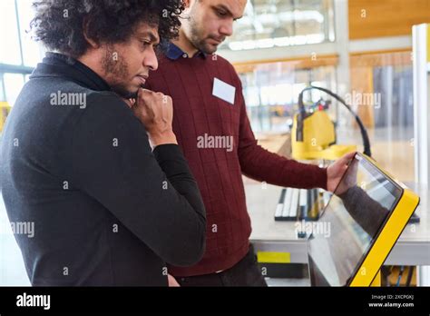 Two Engineers Focused On Programming A Robotic Arm In A Modern Industrial Setting The Image