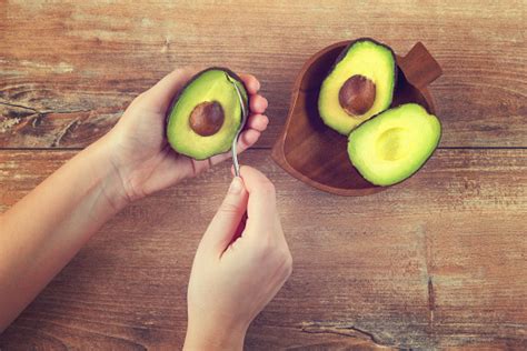 여성의 손은 숟가락을 들고 신선한 잘 익은 아보카도의 절반 여자 필 링 아보카도 나무 테이블에 녹색 아보카도 건강 한 에코 푸드 유기농 재배 제품 갓 수확 한 과일