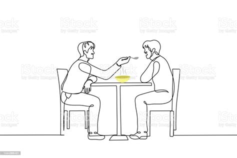 man sits at a table and feeds from a spoon another man sitting opposite