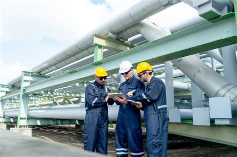 와이드 샷 3 명의 엔지니어 또는 공장 기술자 작업자 팀이 석유 화학 가스 파이프 라인 근처에 서서 태블릿을 사용하여 작업에 대해 논의합니다 25 29세에 대한 스톡 사진