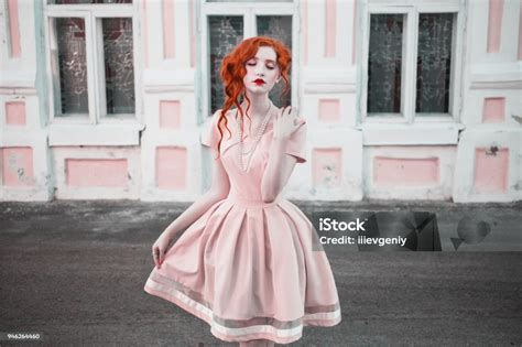 빈티지 배경 창에 복숭아 드레스에 붉은 곱슬 머리를 가진 여자 창백한 피부 파란 눈 밝은 특이 한 모양을 하 고 붉은 입술과 그녀의 목에 구슬와 얇은 허리와 빨간 머리 소녀