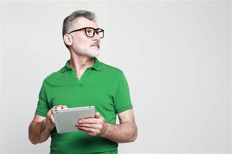 잘 생긴 성숙한 남자의 사진 녹색 티셔츠와 안경을 착용 밝은 회색 배경 위에 태블릿 Pc를 사용 50 54세에 대한 스톡 사진 및 기타 이미지 Istock