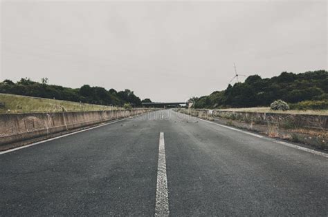 Empty Highway With Wind Turbine And Overpass In Distance On Overcast