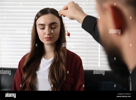 Psychologist using pendulum while working with patient during hypnosis session indoors, closeup ...