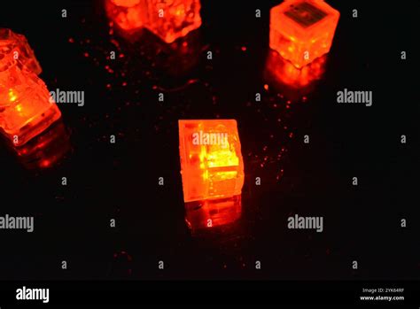 Red Glowing Ice Cubes Are Located On A Black Glossy With Water Drops Plastic Things Made In The