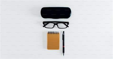 A Pair Of Glasses Pen And Notebook On A White Surface Photo Desk Essentials Image On Unsplash