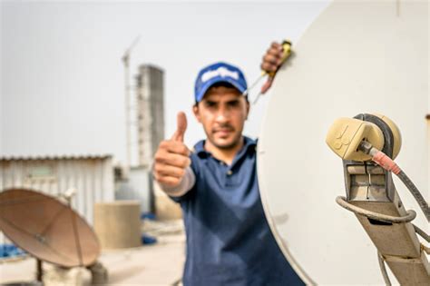 전문 전기 기술자는 지붕 상단에 위성 접시 안테나를 고정 하 고 파란색 유니폼과 캡을 착용 한 후 엄지 손가락을 포기 하 고 도시는 배경에 Stem 주제에 대한 스톡 사진