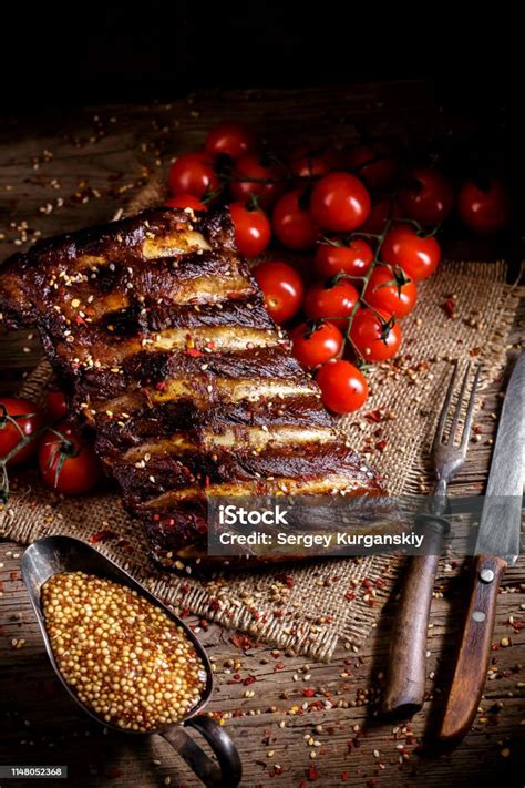 소박한 빈티지 나무 테이블 고기를 곁들인 육즙이 많은 돼지 갈비 체리 토마토 향신료 포크와 나이프 후추 로즈마리 바 질 등 어두운 배경 겨자 상단 사이드 뷰 샷 0명에 대한