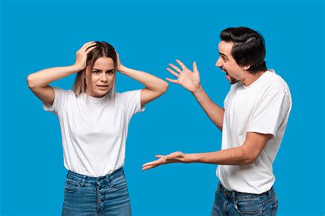 젊은 금발의 여성과 브루넷 수염 남자의 부부는 흰색 티셔츠와 파란색 배경 위에 고립 된 서 서 서 서 서 있는 흰색 티셔츠와 청바지에 콧수염을 가진 남자 2명에 대한 스톡