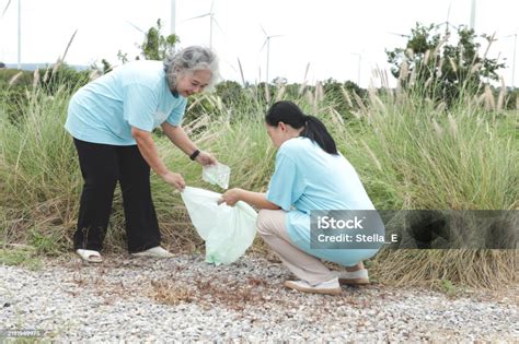 두 명의 나이 지긋한 아시아 여성이 풍력 터빈 농장에서 쓰레기를 수거하는 자원봉사자 자원 봉사자는 풍력 터빈 공원을 배경으로 쓰레기 수거로 초원을 청소합니다 생태 및 환경
