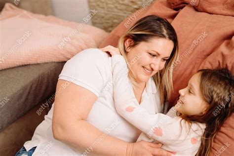 Daughter And Mother Lying Down On Big Pillow Hugging Each Other With