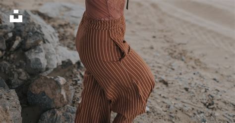 낮 동안 갈색 모래 위에 서 있는 검은 모자를 쓰고 갈색과 검은색 줄무늬 드레스를 입은 여자 사진 Unsplash의 무료