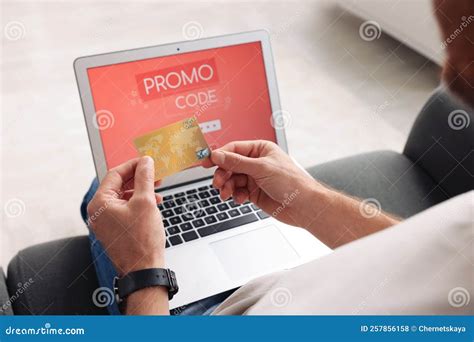 Man Holding Laptop With Activated Promo Code And Credit Card On Sofa