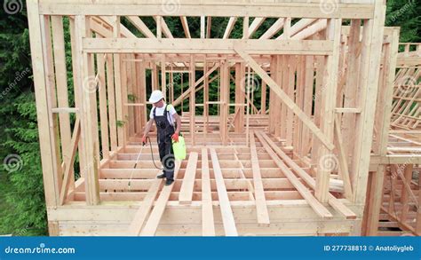 Worker Applying Fire Retardant Using Sprayer While Constructing Wooden Frame House Near Forest