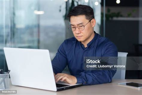 현대 사무실에서 일하는 진지한 생각의 아시아 사업가 직장에서 노트북을 사용하는 셔츠와 안경을 쓴 성숙한 남자 복잡한 결정을 숙고하는 투자자 35 39세에 대한 스톡 사진 및