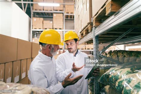 유니폼과 이야기 하는 머리에 헬멧에 두 노동자에 대 한 저장소에 서 있는 동안 작동합니다 도처에 상자 젊은 노동자 지주 타블렛 가정의 방에 대한 스톡 사진 및 기타 이미지