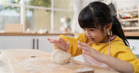 부엌에서 수제 빵집을 하는 아시아 어린 소녀의 초상화 사랑스러운 어린 아이가 테이블에 앉아 행복을 느끼고 집에서 손으로 음식을 요리하거나 반죽 효모 반죽을 굽는 법을