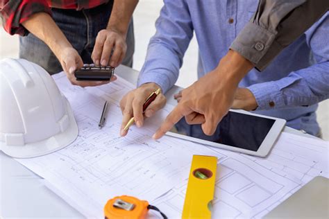 파란 글씨로 건설 현장에서 일하는 엔지니어와 건축가의 건설 개념 컴퓨터 노트북 계산기로 건설 계획을 논의하는 엔지니어와 건축가 3 명에 대한 스톡 사진 및 기타 이미지