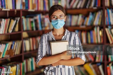 책을 들고 얼굴 마스크와 도서관에 서 젊은 매력적인 대학생의 초상화 코로나 바이러스 개념 중 공부 도서관에 대한 스톡 사진 및