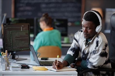 Premium Photo Serious Programmer In Headphones Making Notes In
