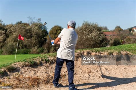 뒤에서 보이는 나이 지긋한 골퍼가 모래 벙커에서 그린을 향해 능숙하게 공을 치고 있다 경기 스포츠에 대한 스톡 사진 및 기타 이미지 경기 스포츠 경쟁 골프 Istock