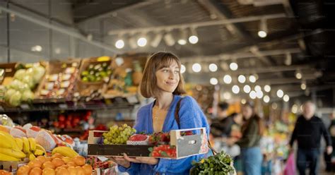 젊은 쾌활한 여자의 초상화는 현지 시장에서 신선한 과일과 열매로 가득 찬 상자를 들고 있습니다 시장에서 음식을 사는 여자 현지 제품의 전통적인 오프라인 소매 개념 사진