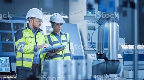 공장 워크샵 전문 여성 엔지니어 남성 기계 작업자는 산업 용 디지털 태블릿 컴퓨터를 사용하여 작업하고 생산 라인을 위한 로봇 암을 프로그래밍합니다 Cnc 기계가 있는 첨단