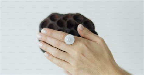 흰색 바탕에 말린 연꽃이 있는 아름다운 손에 세련 된 현대 흰색 둥근 반지 흰색 매니큐어로 여성 손에 특이한 유행 융합 유리 반지 에코 및 케어 개념 사진