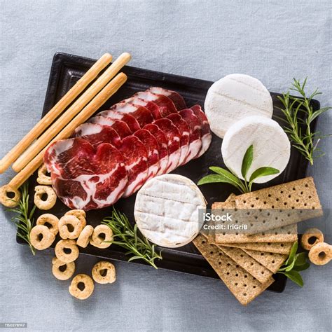 차가운 커트와 치즈는 파란 리넨 축제 식탁보에 향기로운 허브가 있는 화이트 와인 크래커 그리 시 니 및 타 갈리와 테이블의 트레이에 제공 됩니다 고기에 대한 스톡 사진 및
