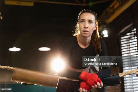 여자 파이터 걸 파워 빨간 권투를 한 여자 파이터는 권투 링에 서서 보호 붕대를 감고 밧줄에 기대어 휴식을 취합니다 강한 강력한 소녀 근력 운동 운동에 적합합니다 스포츠에