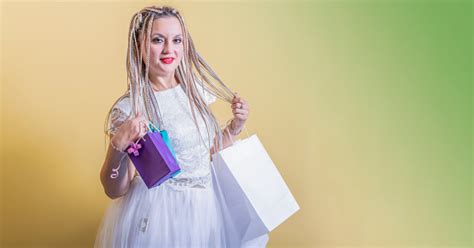 그녀의 머리와 흰색 드레스에 피그 테일을 가진 소녀는 노란색 배경에 서서 그녀의 손에 선물을위한 가방을 들고있다 카메라를 들여다본다 30 34세에 대한 스톡 사진 및 기타