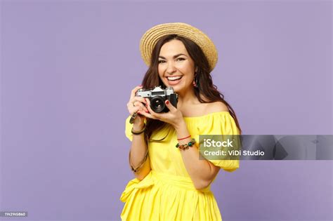 노란 드레스 여름 모자 파스텔 바이올렛 벽 배경에 고립 된 복고풍 빈티지 사진 카메라에 사진을 찍는 쾌활 한 젊은 여자 사람들은