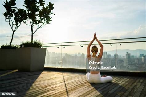 옥상에서 명상 야외명상을 위한 영적 연습 중에 휴식을 취하는 트랙수트에 있는 여성의 뒷모습 요가 포즈에 앉아 있는 활동적인 여성의 젊은 여성이 거대 도시에서 고요하고