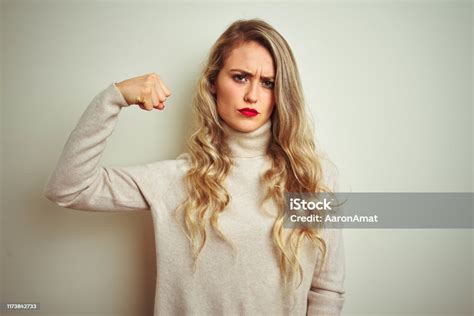 고립 된 흰색 배경 위에 겨울 터틀넥 스웨터를 입은 아름다운 여성은 팔 근육을 보여주는 강한 사람 자신감과 힘을 자랑스럽게 생각합니다 가을에 대한 스톡 사진 및 기타 이미지