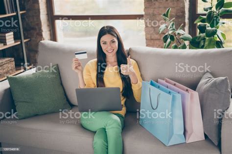 긍정적 인 소녀 학생의 초상화 사용 컴퓨터 플라스틱 카드 쇼핑 구매 추천 표시 처럼 사인 앉아 아늑한 소파 에 집 실내 갈색