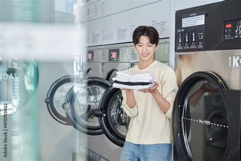 Zdjęcie Stock 셀프 서비스 세탁실에서 빨래를 세탁기와 건조기를 작동하며 빨래를 정리하고 있는 젊은 아시아 한국남자 모델 Adobe Stock