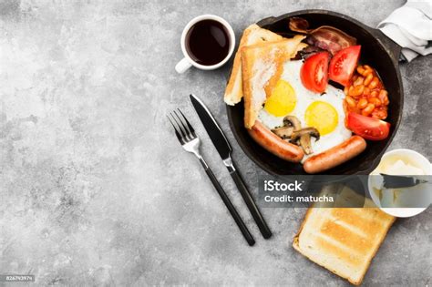전통적인 영국식 아침 식사베이컨 소시지 달걀 프라이 토마토 콩 버섯 버터요리 냄비 및 회색 배경에 커피에 토스트 보기 상위