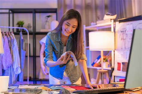 아시아 성인 여성 패션 디자이너 천 재단사 새로운 컬렉션 스케치 드로잉을 위해 일하는 새로운 색상 견본 직물 샘플을 밤에 디자인 스튜디오 홈 스튜디오의 책상에서 선택합니다