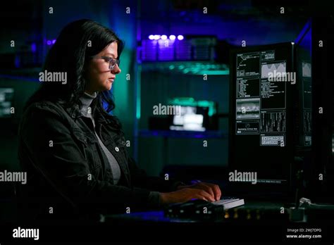 Low Key Lighting Shot Of Female Computer Hacker Sitting In Front Of Screens Breaching Cyber