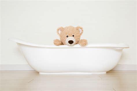 밝은 회색 벽 배경에 나무 바닥에 있는 집 방에서 흰색 플라스틱 욕조에서 보고 있는 웃는 갈색 테디 베어 근접 촬영 아기 목욕 개념입니다 앞 모습 0명에 대한 스톡 사진 및
