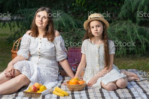 공원의 어머니와 딸은 작은 피크닉을 하 고 있습니다 그들은 식사를 위한 과일과 타탄 격자 무늬에 앉아 있다 건강 한 라이프 스타일과 식물성의 개념 가족에 대한 스톡 사진 및