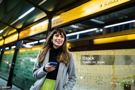 버스를 기다리는 동안 스마트 폰을 들고 멀리 바라 보는 행복한 젊은 여성 지하철 철도에 대한 스톡 사진 및 기타 이미지 지하철 철도 부에노스아이레스 한 명의 여자만
