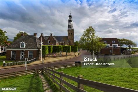 네덜란드 Hindeloopen 해안 잔디로 자란 높은 해안 벽 길 중간에 집과 높은 탑이 있는 교회로 가는 길로 이어집니다 역동적인 구름이 있는 하늘 네덜란드에 대한 스톡