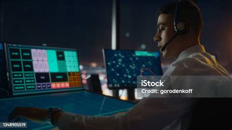 공항 타워에서 전화에 헤드셋 토크와 남성 항공 교통 컨트롤러 사무실 방은 내비게이션 화면 비행기 출발 및 팀의 도착 데이터가있는 데스크톱 컴퓨터 디스플레이로 가득합니다 항공