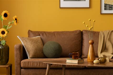 모형 포스터 프레임 갈색 소파 나무 커피 테이블 녹색 잎이 달린 꽃병 베개 노란색 벽 및 개인 액세서리로 거실 인테리어의 창의적인 구성 가정 장식 템플렛 0명에 대한 스톡