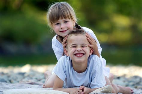 두 젊은 행복 한 귀여운 금발 미소 어린이 소년과 소녀 형제와 자매 흐리게 밝은 화창한 여름 날 배경에 자갈 해변에 누워 우정과